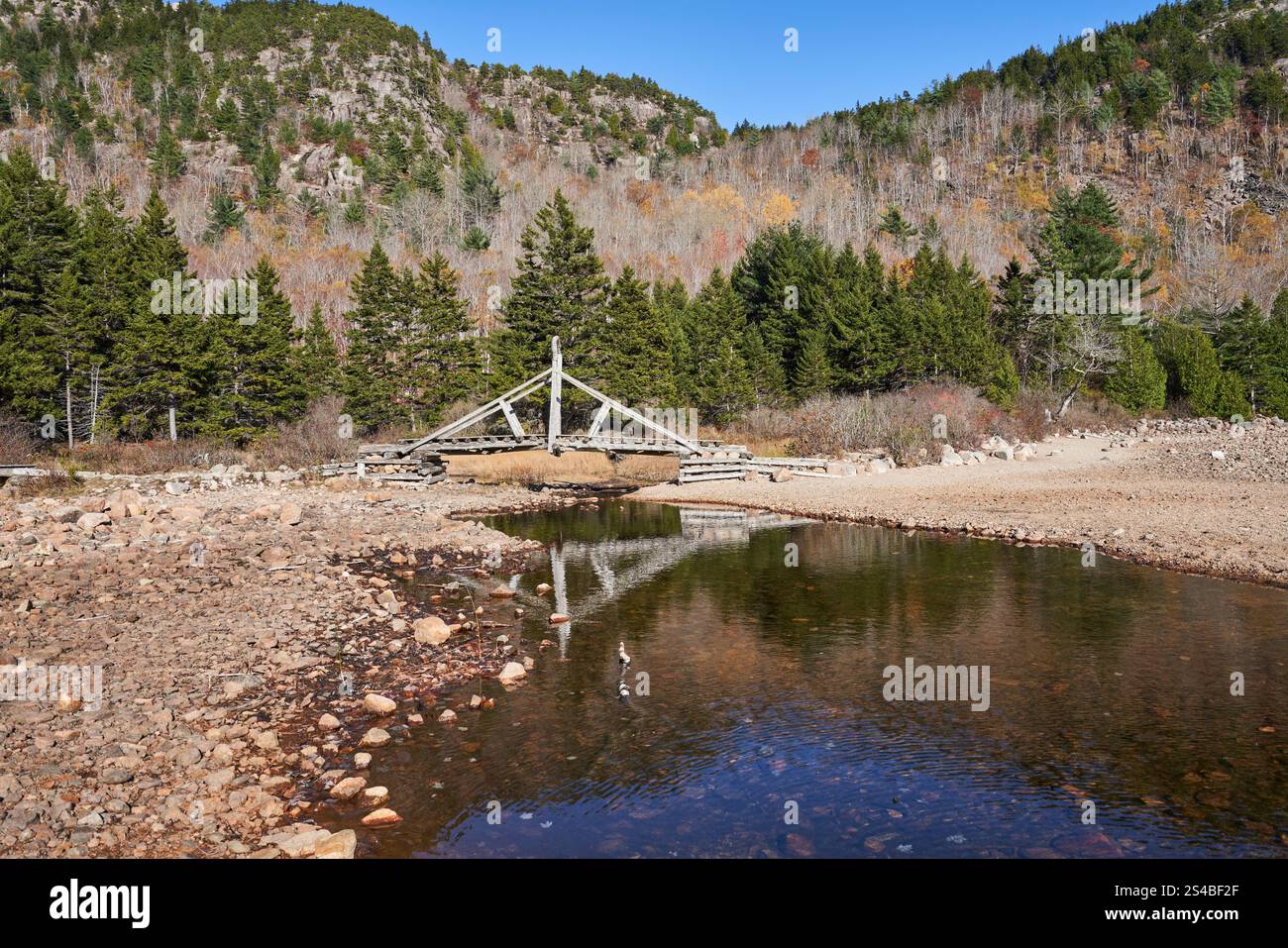 A rustic, old-fashioned bridge crosses a creek. The trail surrounds ...