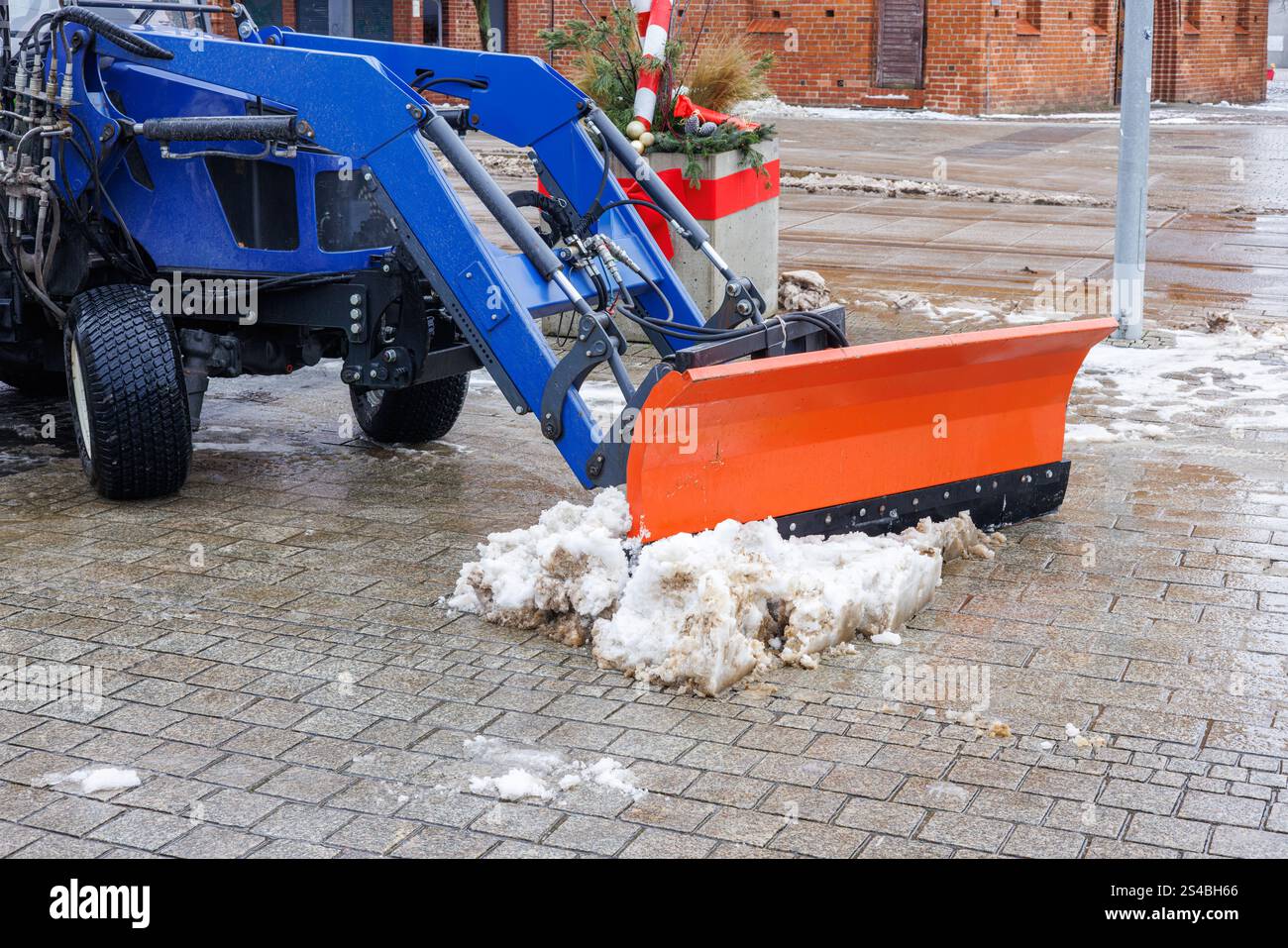 Front of a blue tractor with an orange bucket removing snow in a town ...