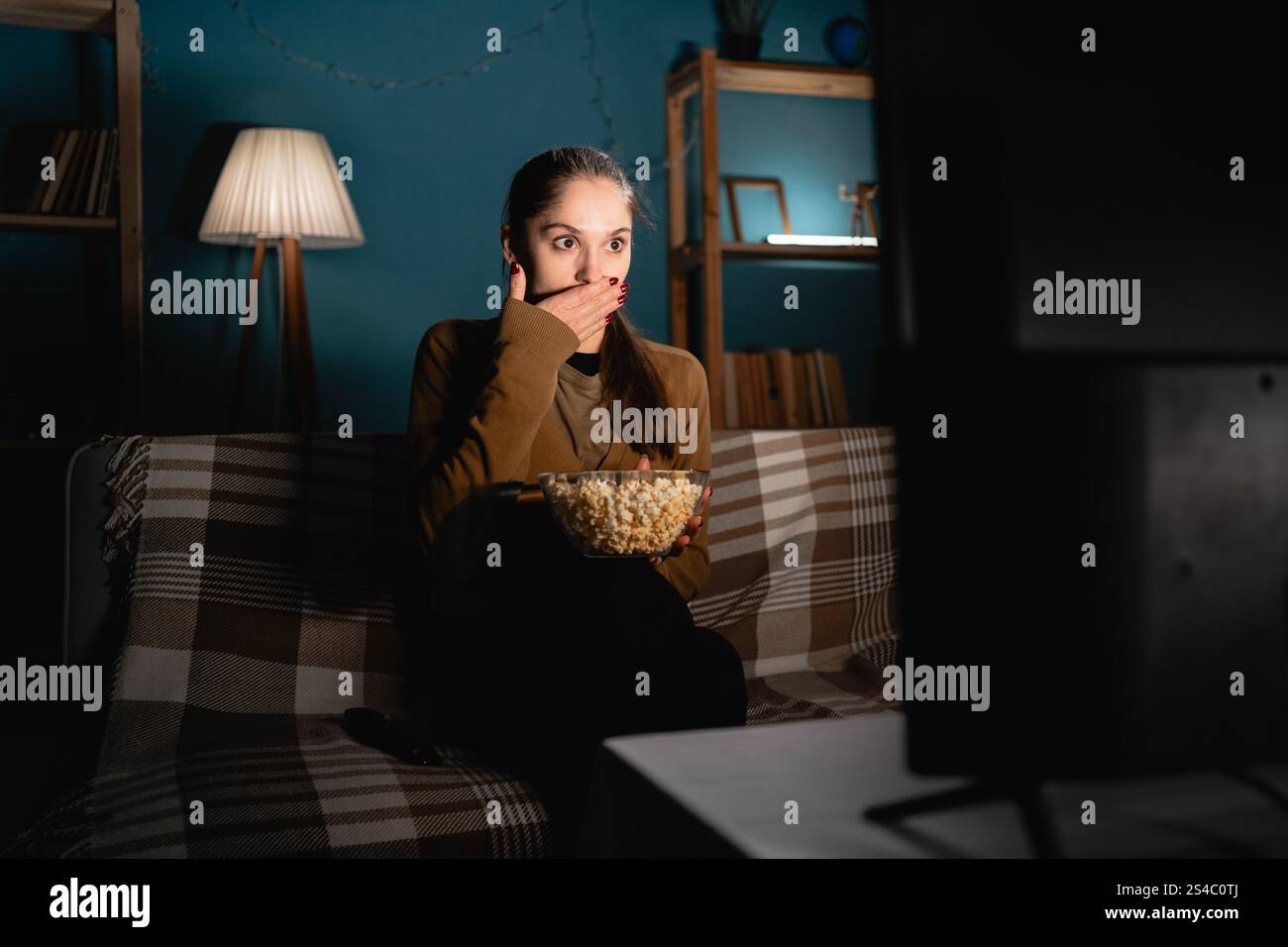 Shocked woman watching scary movie covers mouth in shock sitting near ...