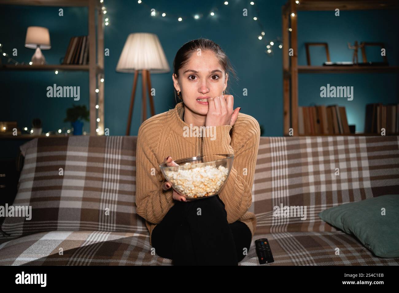 Nervous female spectator bite nails watching tv and eating popcorn at ...