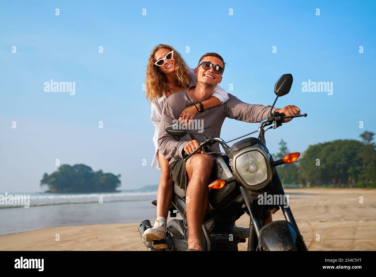 Couple rides motorbike on beach. Man drives motorcycle, woman hugs ...