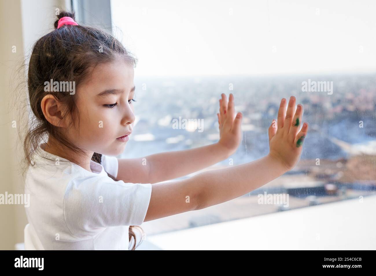 Beautiful little girl smiling and watching out the window. A child ...