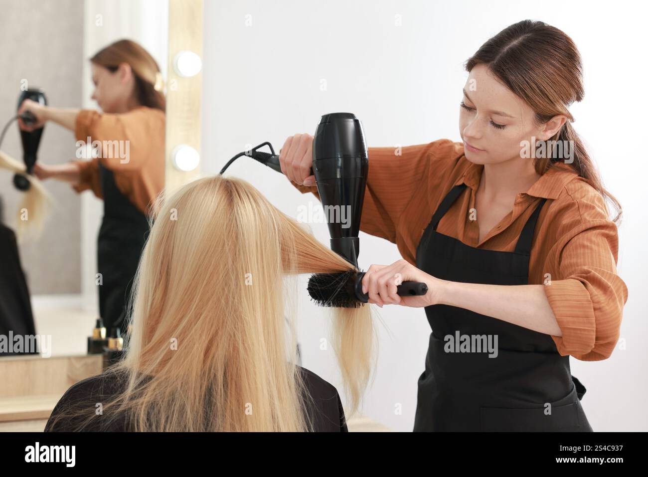 Hairdresser blow drying client's hair in salon Stock Photo - Alamy