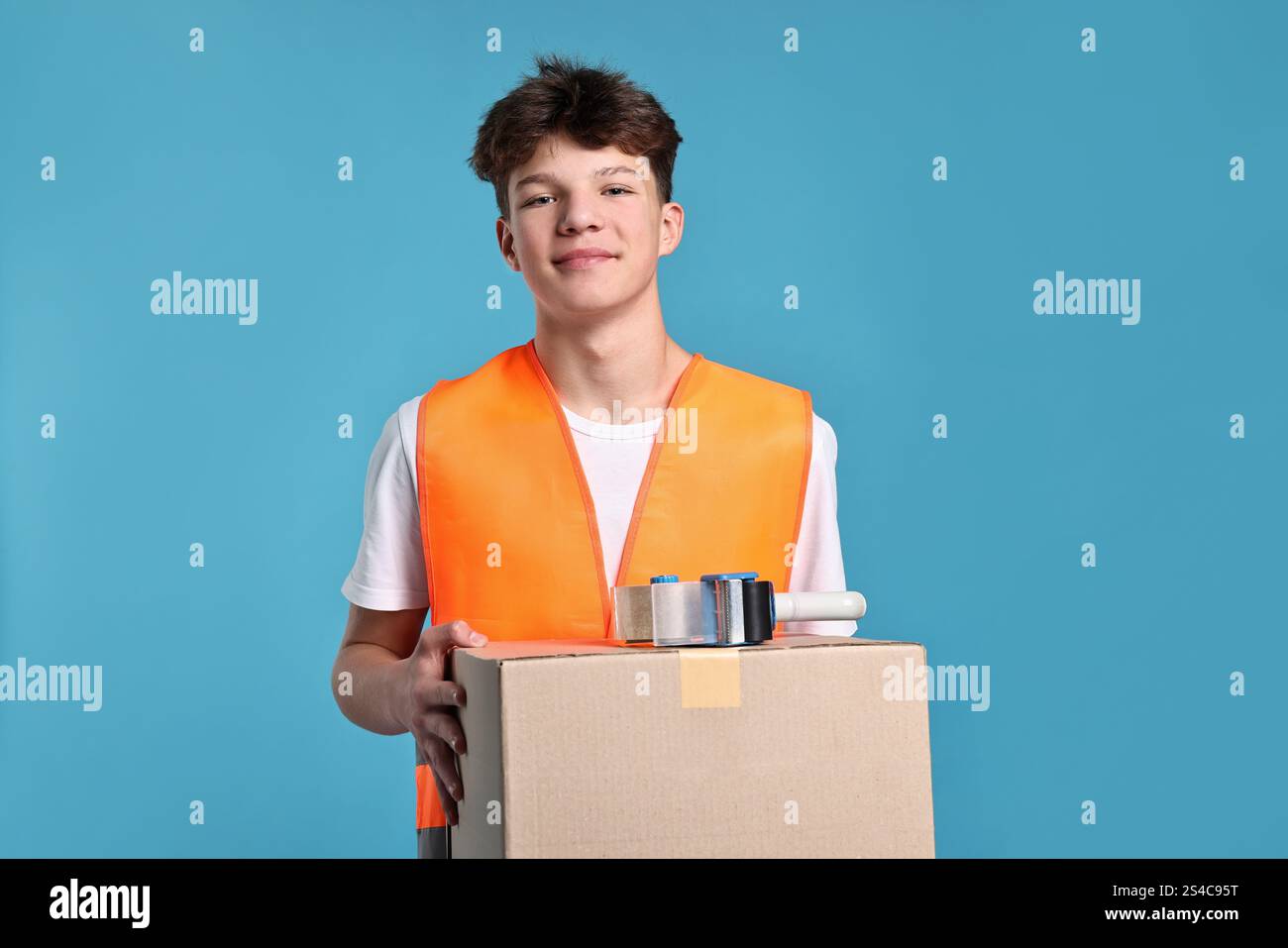 Teenage boy with tape gun dispenser and box in safety vest working as ...