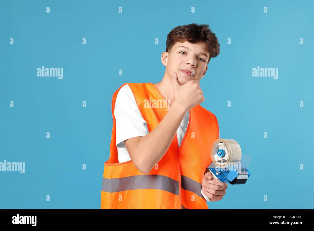 Teenage boy with tape gun dispenser in safety vest working as warehouse ...