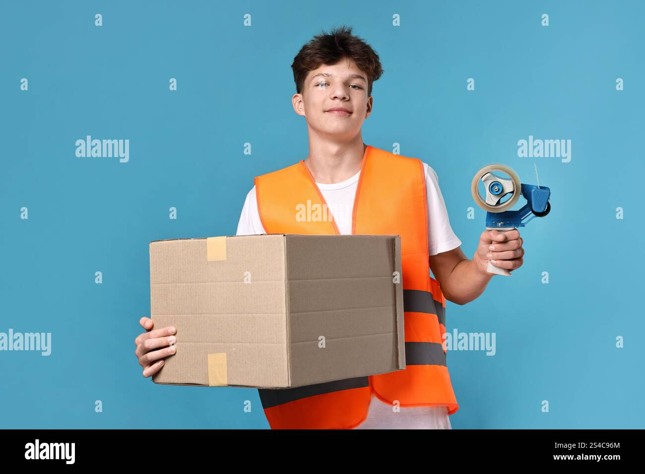 Teenage boy with tape gun dispenser and box in safety vest working as ...