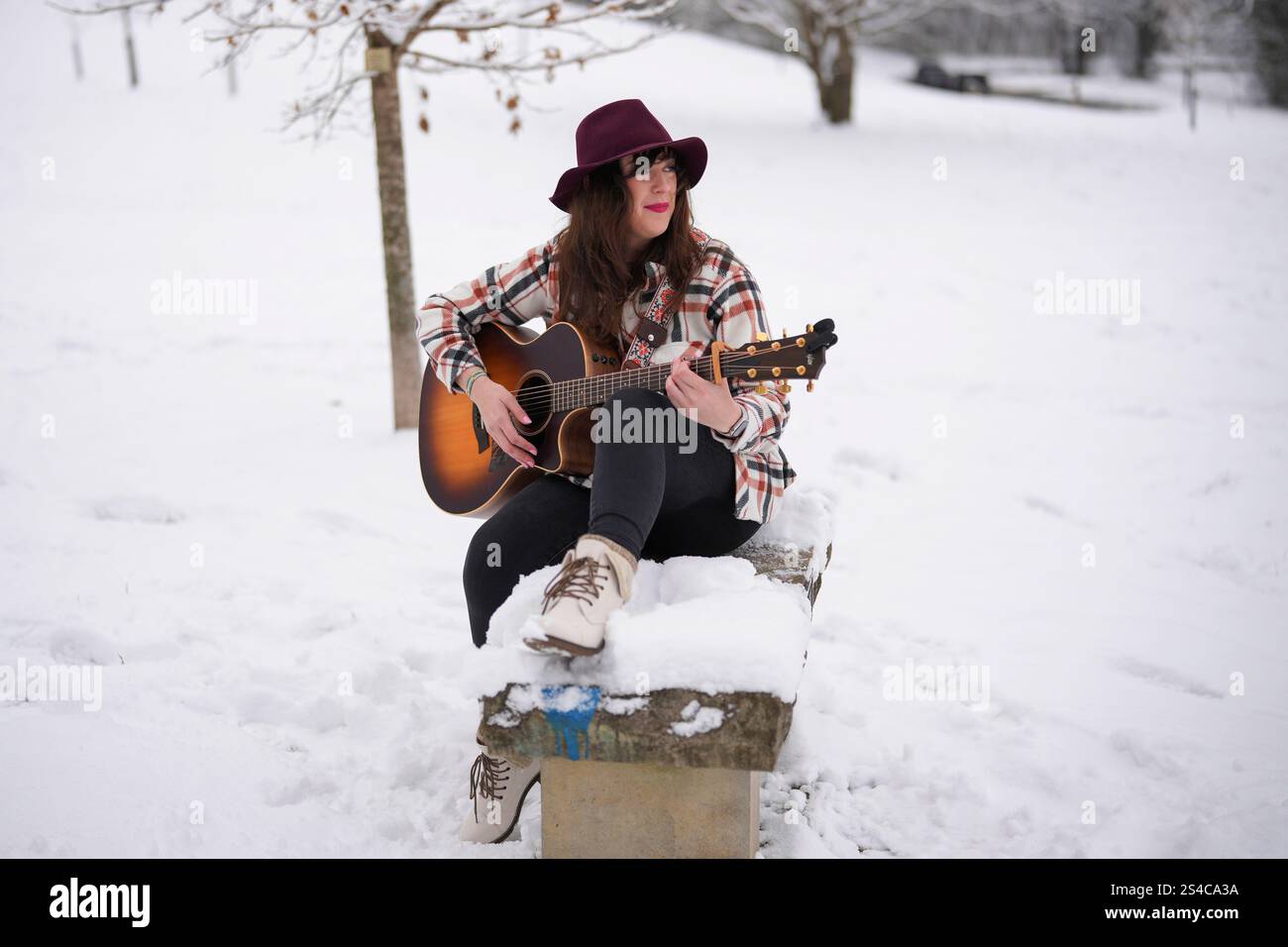 Victoria Collings plays her guitar as she sits on a bench in the snow ...