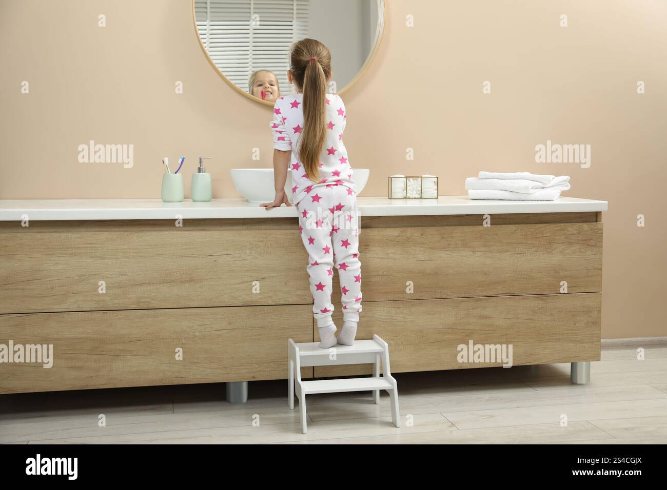 Little girl with toothbrush standing on step stool near bathroom vanity ...