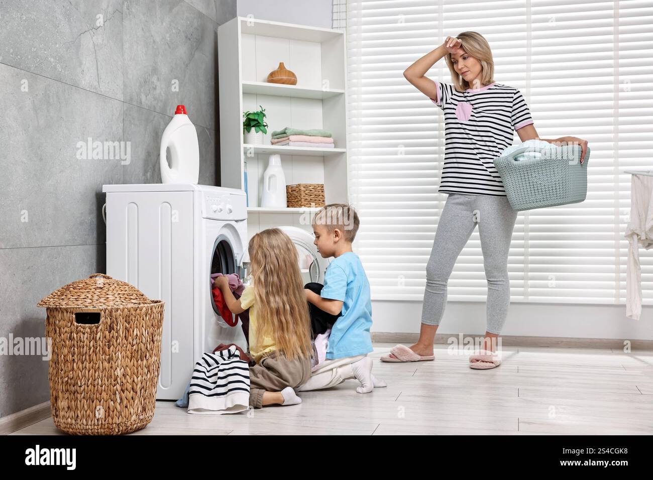 Tired housewife and her kids doing laundry together in bathroom Stock ...