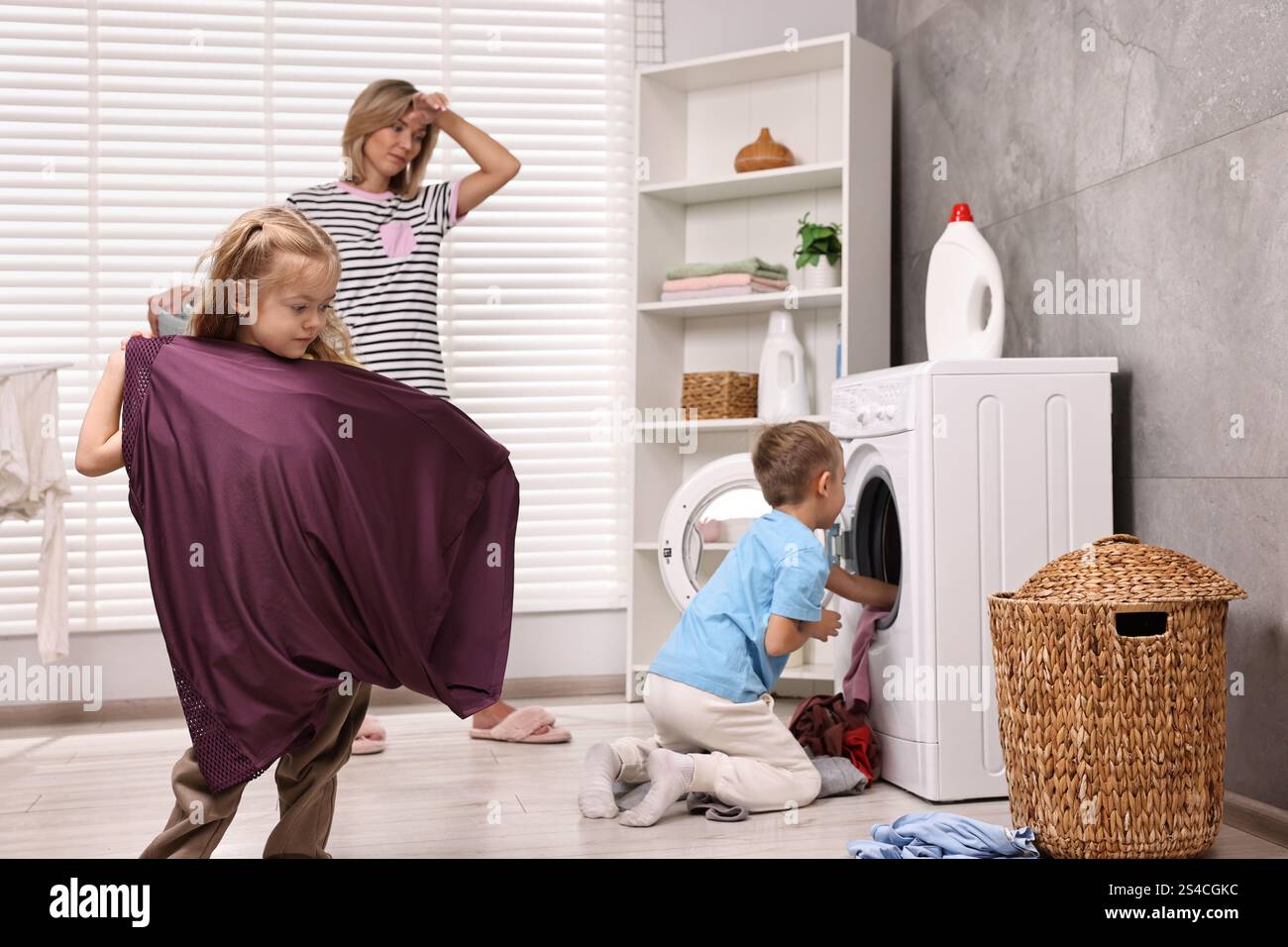 Tired housewife and her kids doing laundry together in bathroom Stock ...