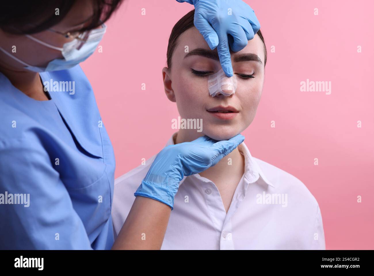 Doctor checking patient's nose after plastic surgery operation on pink ...