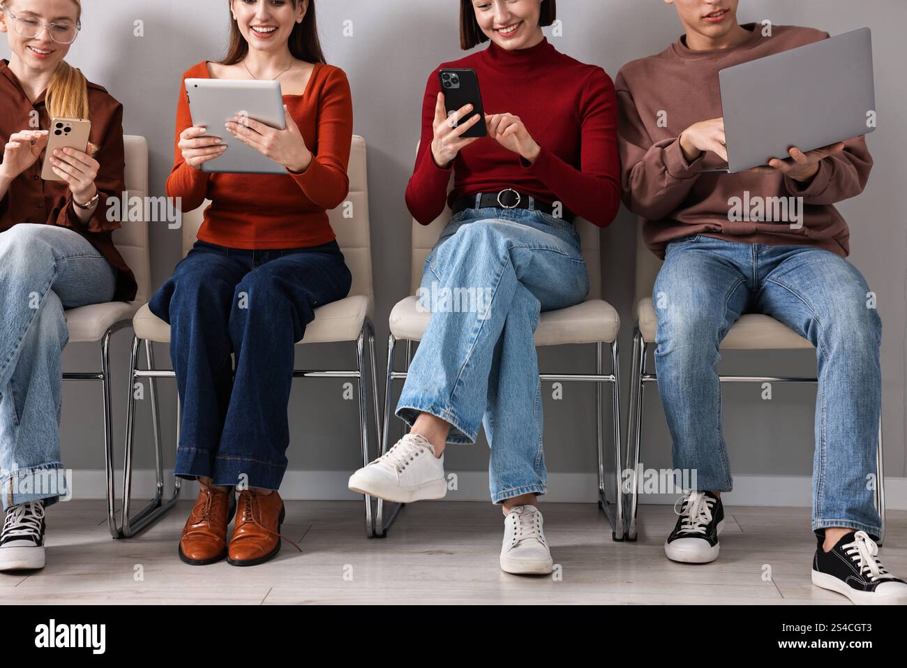Group of people using different gadgets on chairs near grey wall ...