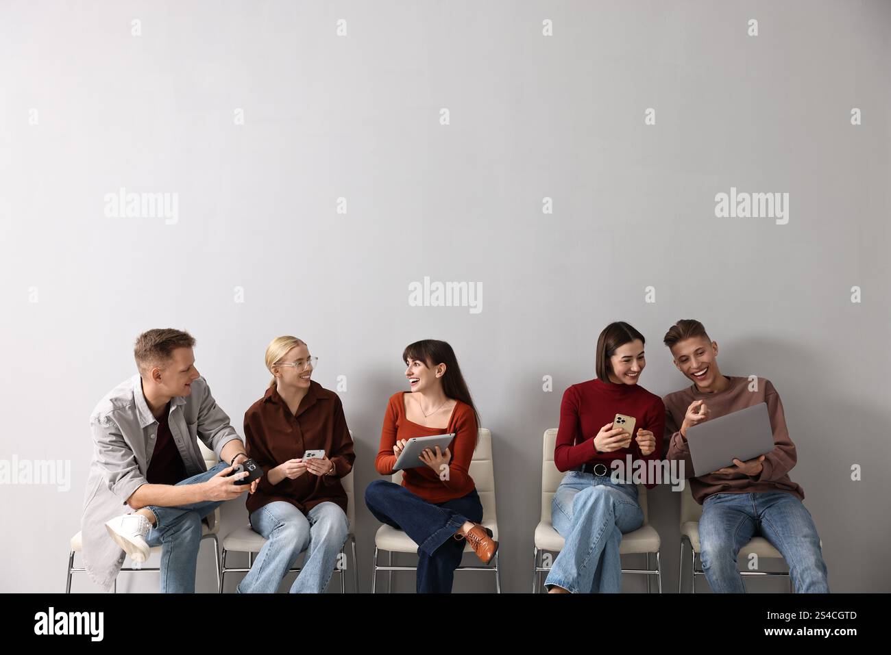 Group of people using different gadgets on chairs near light grey wall ...