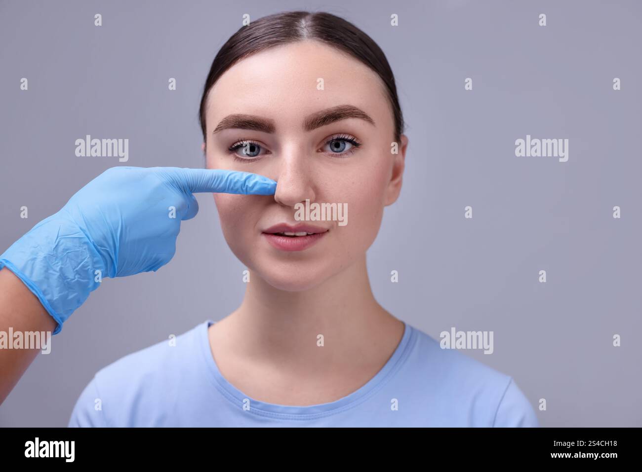 Doctor checking patient's nose before plastic surgery operation on grey ...