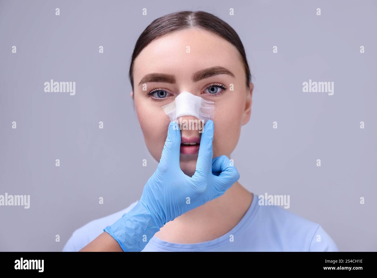 Doctor checking patient's nose after plastic surgery operation on grey ...