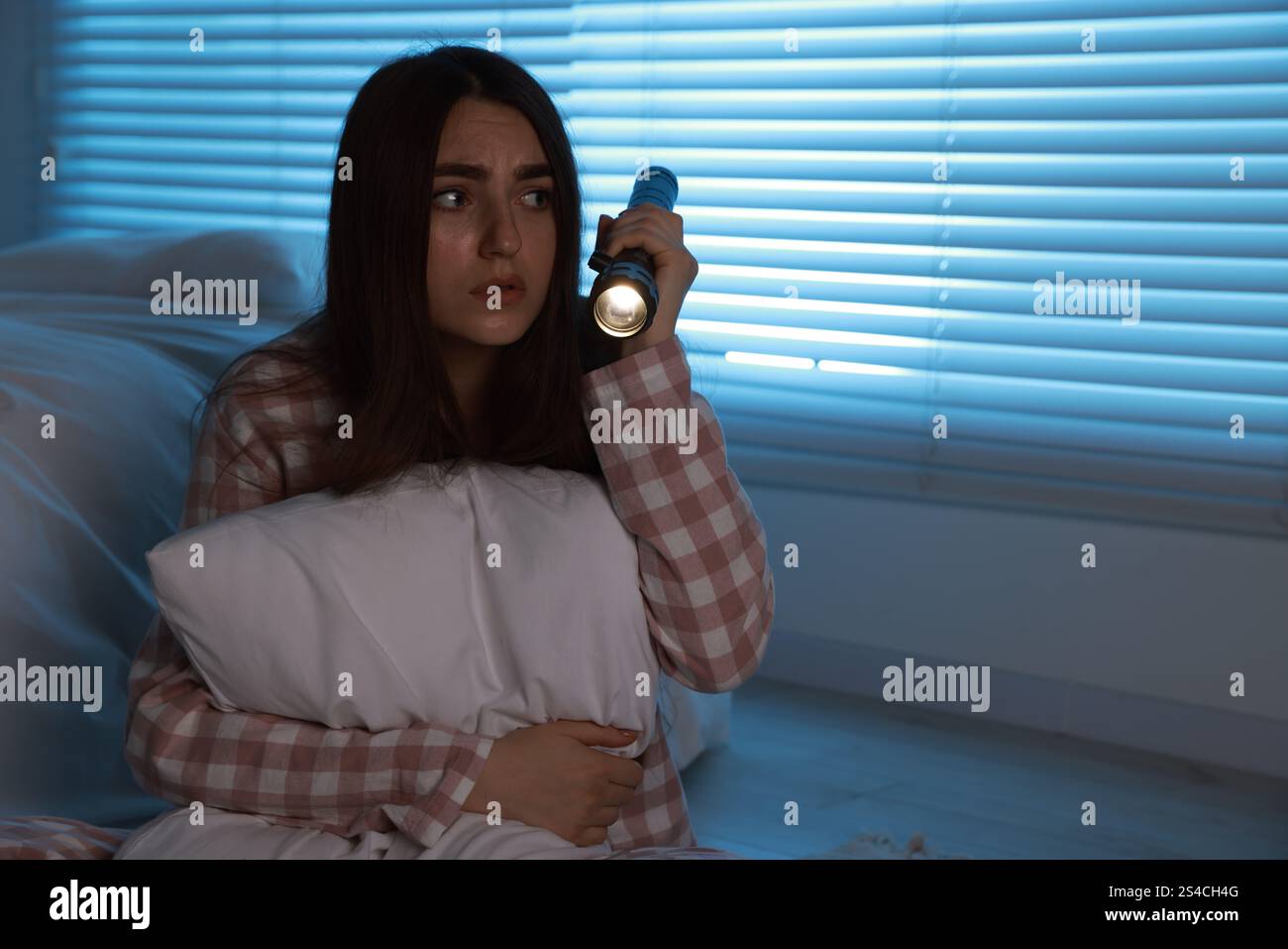 Fear of darkness. Scared young woman with flashlight hugging pillow in ...