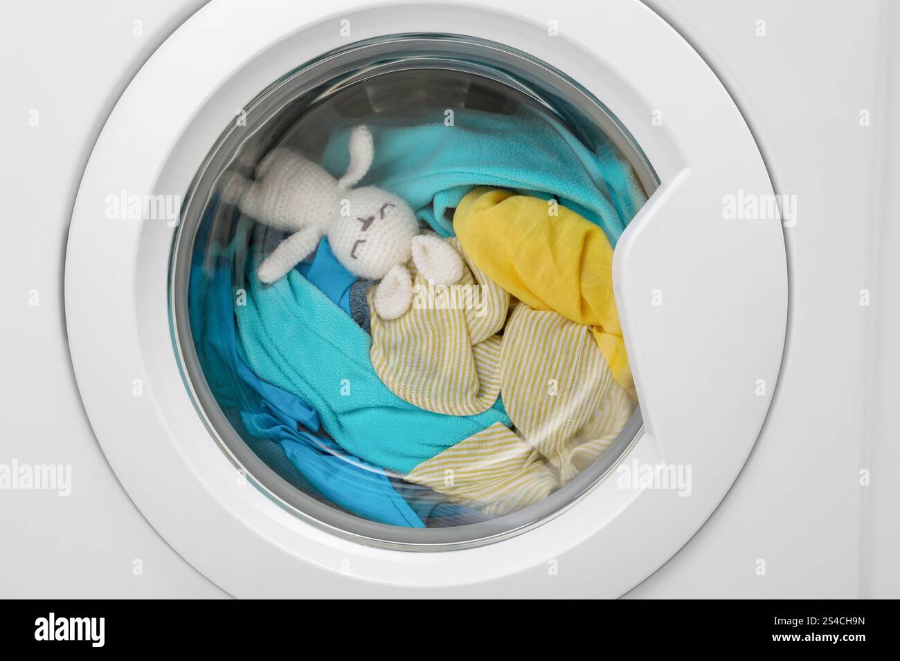 Washing machine with clothes and toy bunny as background, closeup Stock ...