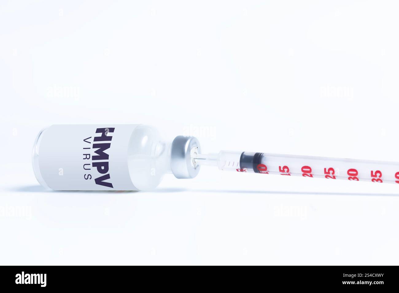 A medical syringe and HMPV vaccine bottle arranged on a white ...