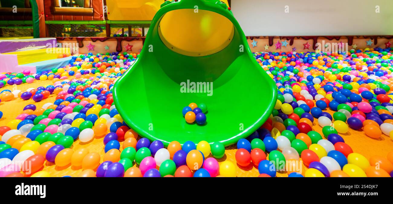 A green slide leading into a colorful ball pit in a vibrant indoor ...