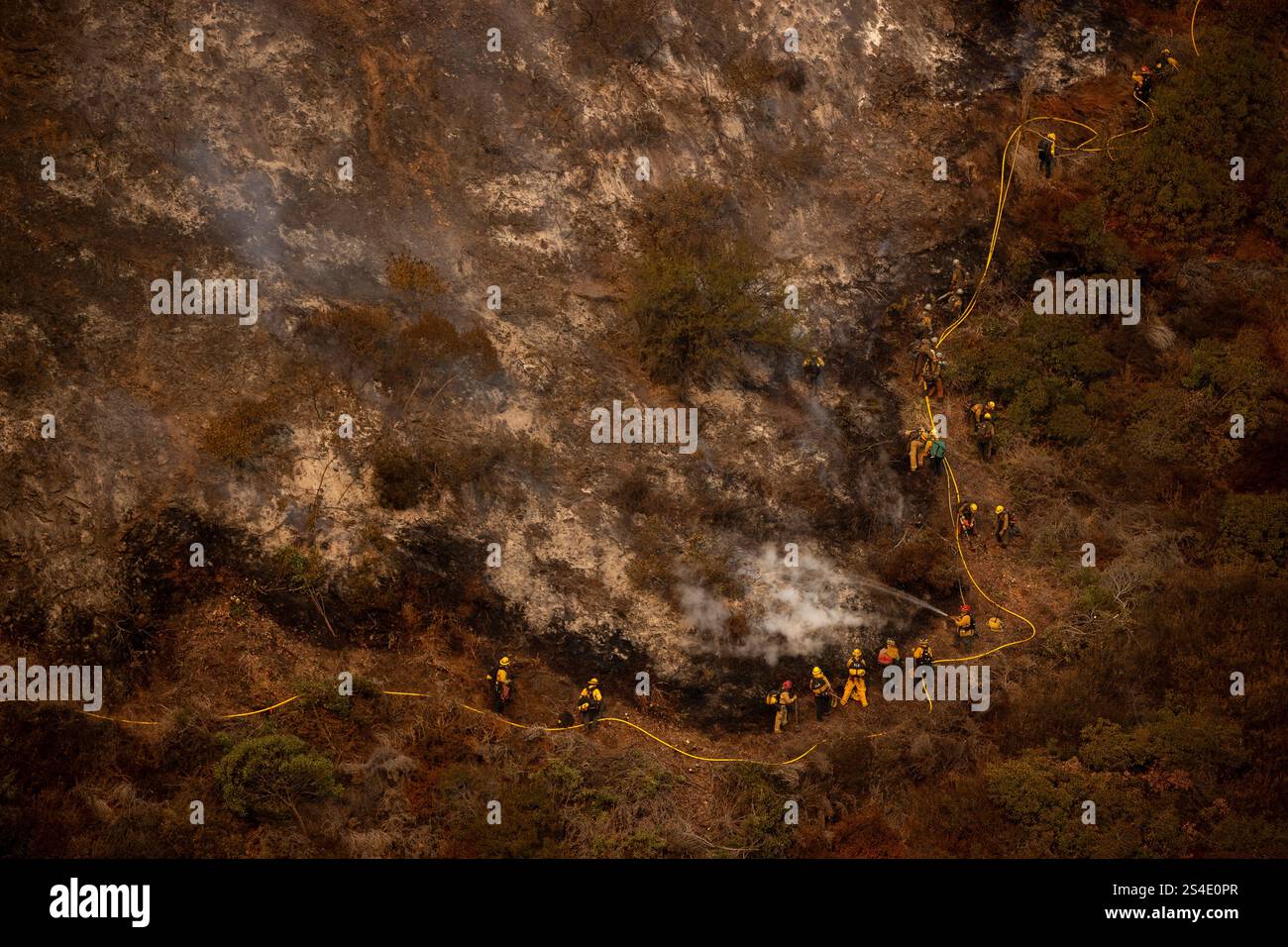A group of firefighters traverse a steep hill while battling the ...