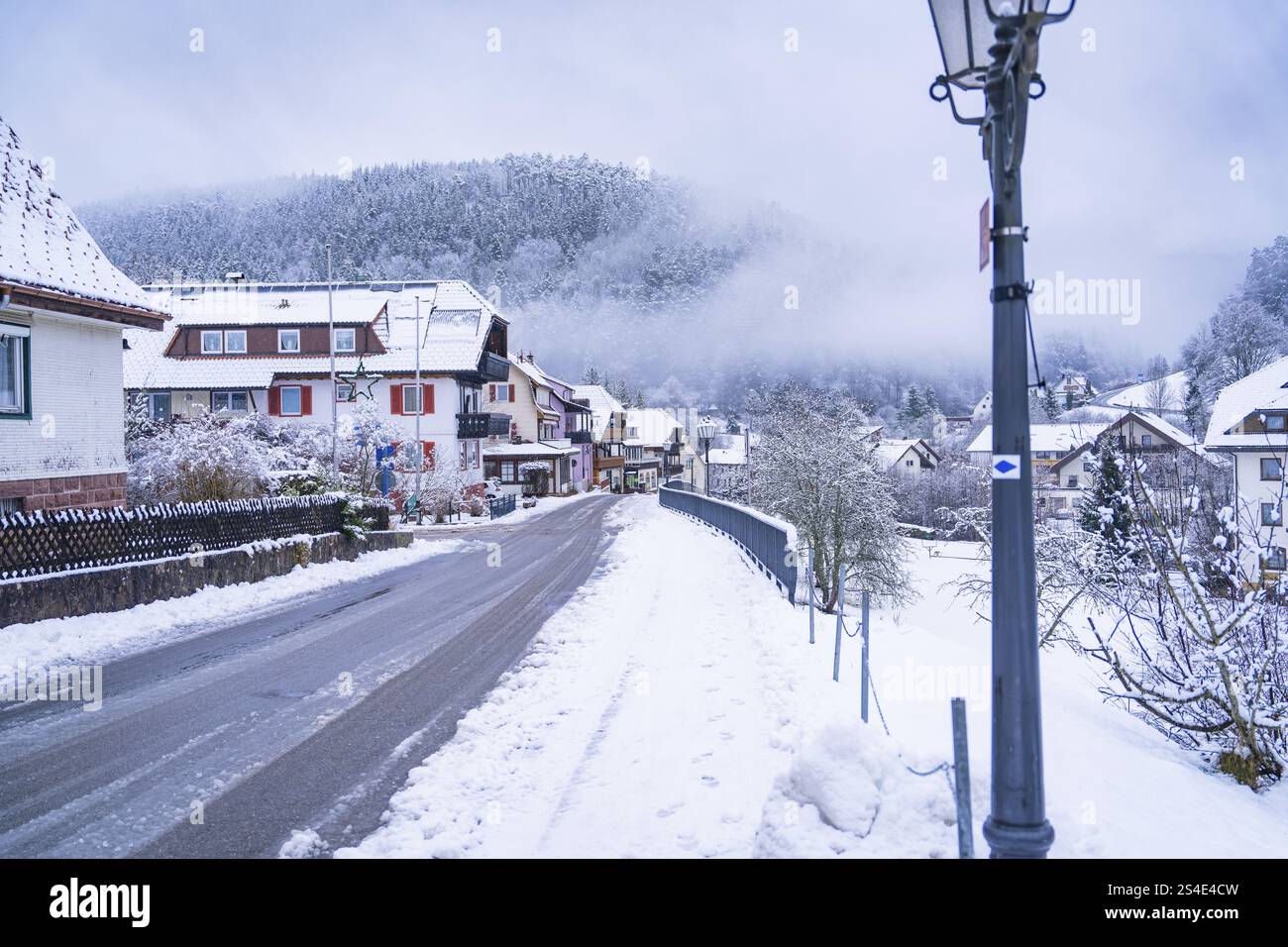 Snow-covered village street with houses and lanterns, surrounded by fog ...