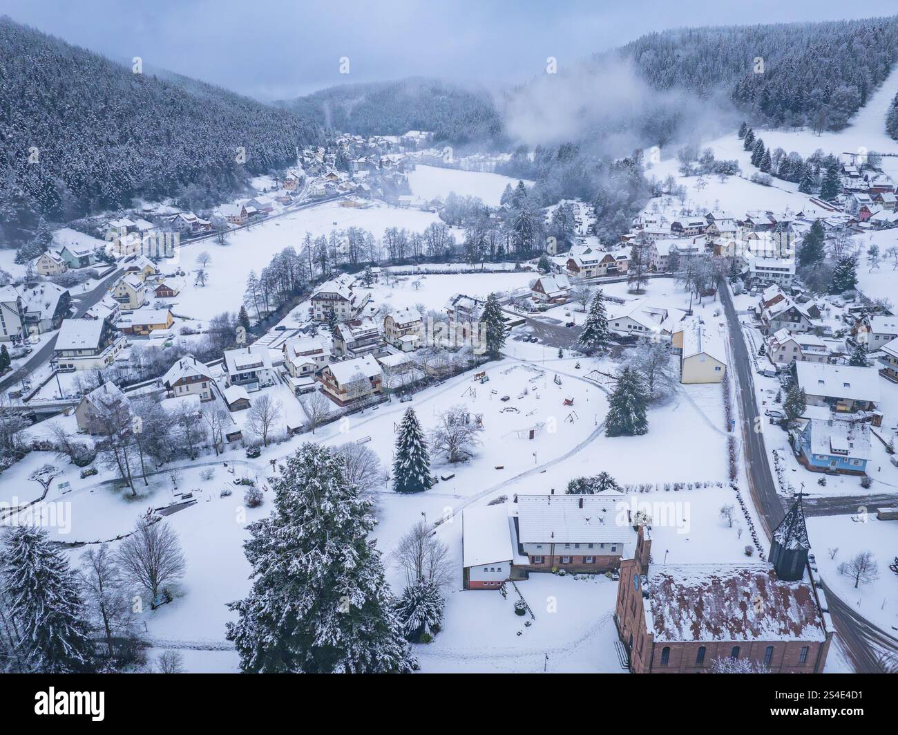 Snow-covered village in a valley surrounded by wooded hills ...