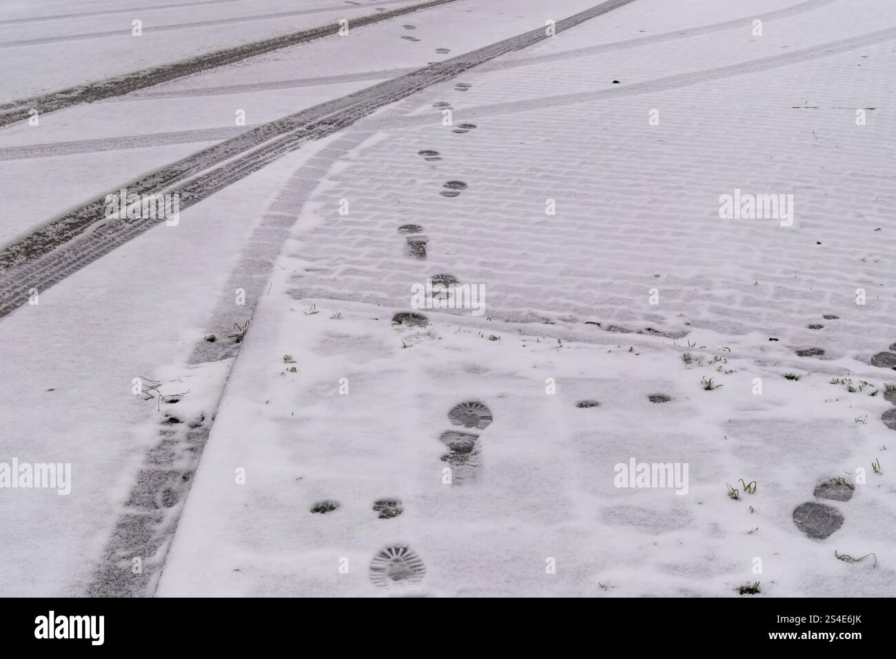 Fresh snow covers a cobblestone street with footprints and tire tracks ...