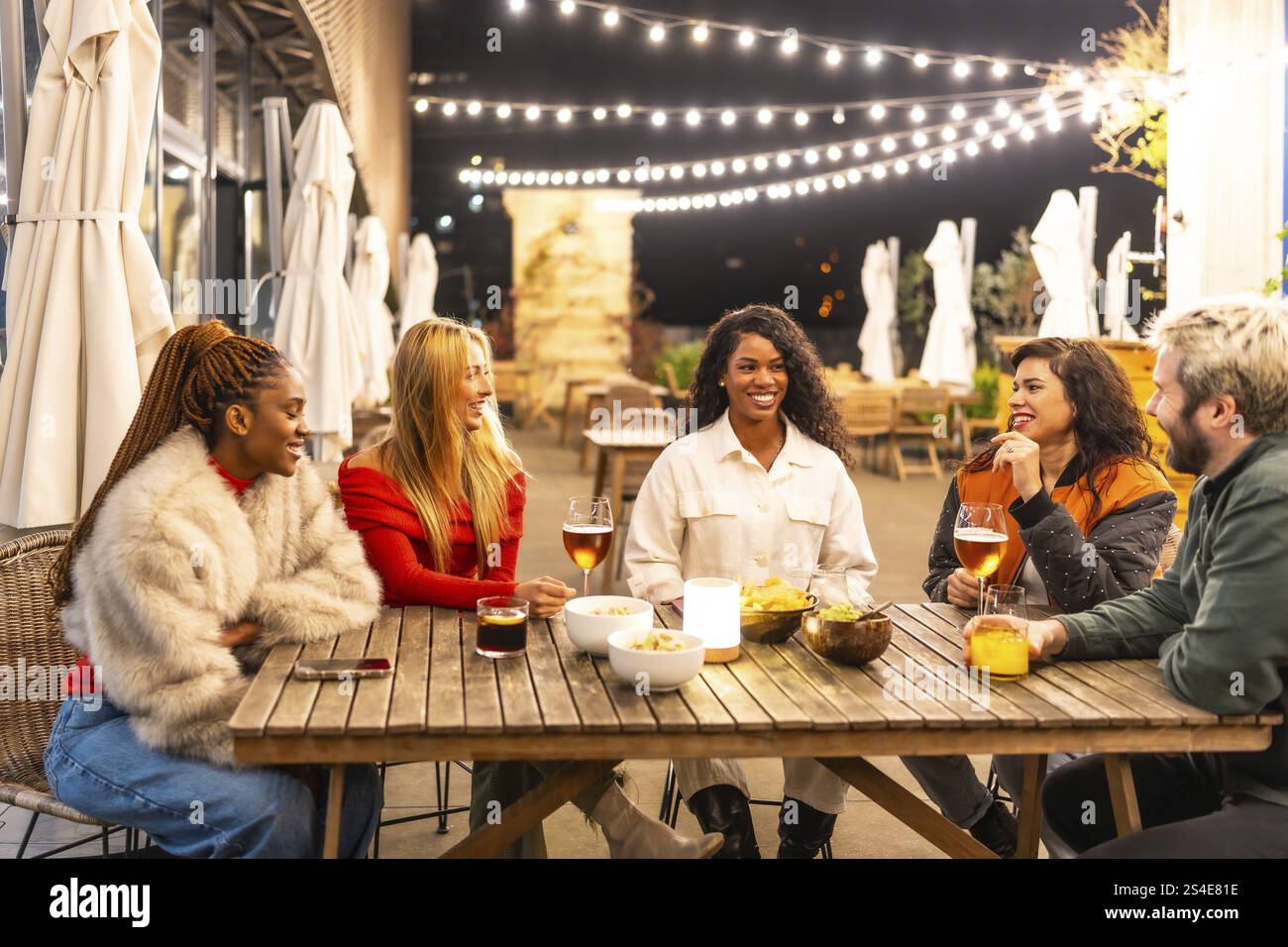 Multi-ethnic friends sitting on a bar terrace drinking celebrating ...
