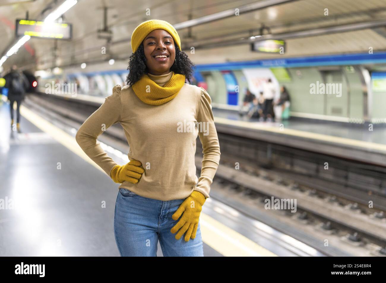 Smiling young woman wearing yellow wool cap and gloves is waiting for ...