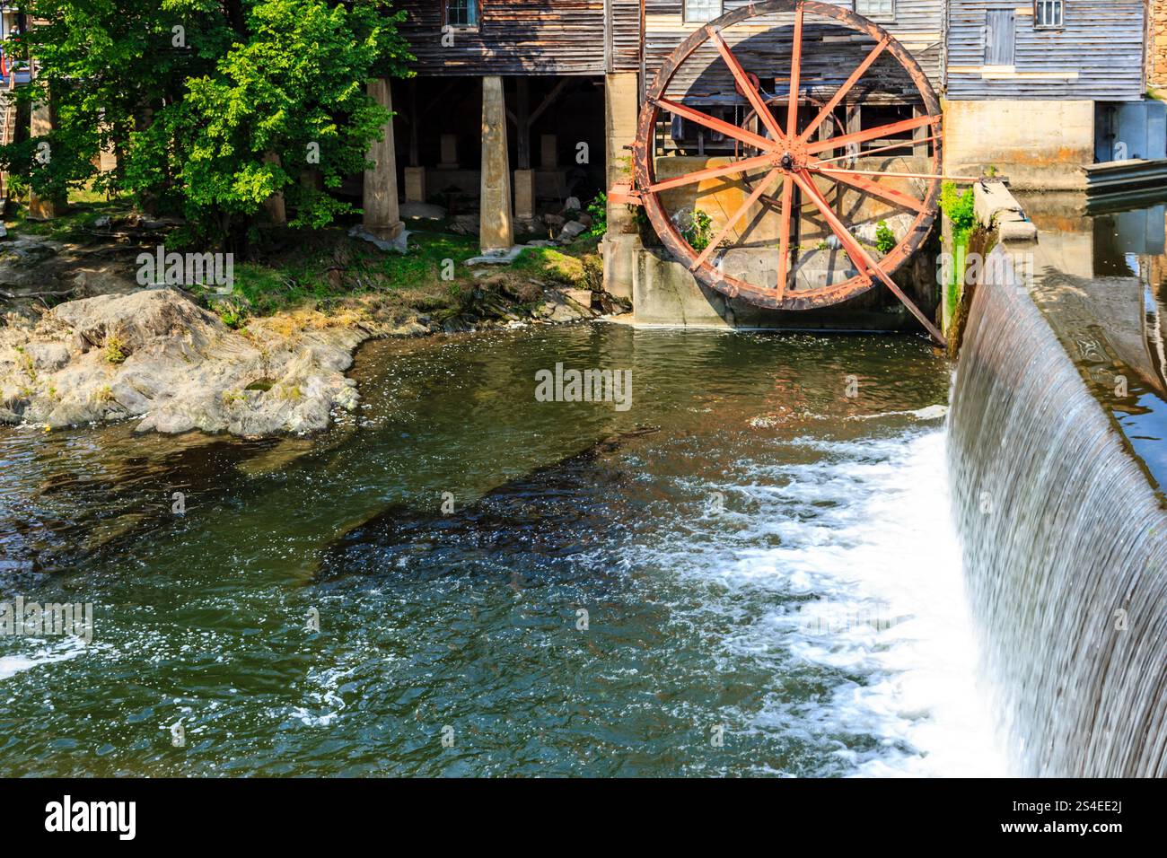 A large water wheel is in the middle of a river. The water is flowing ...