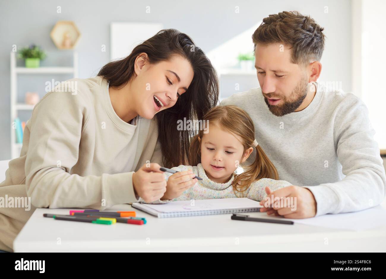 Little cute child girl sitting with parents at home and drawing a ...