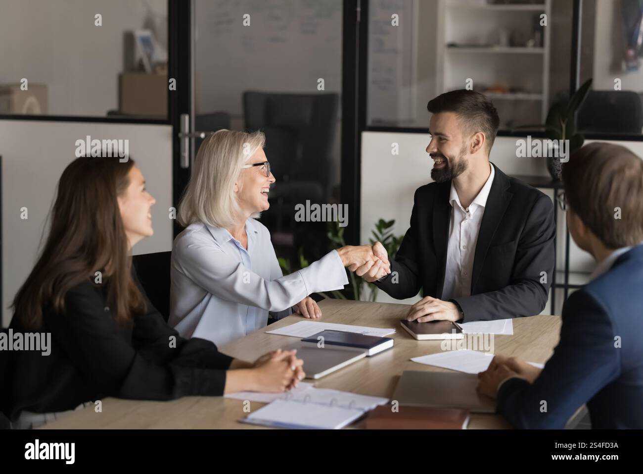 Two teammates shaking hands seated at desk in office Stock Photo - Alamy