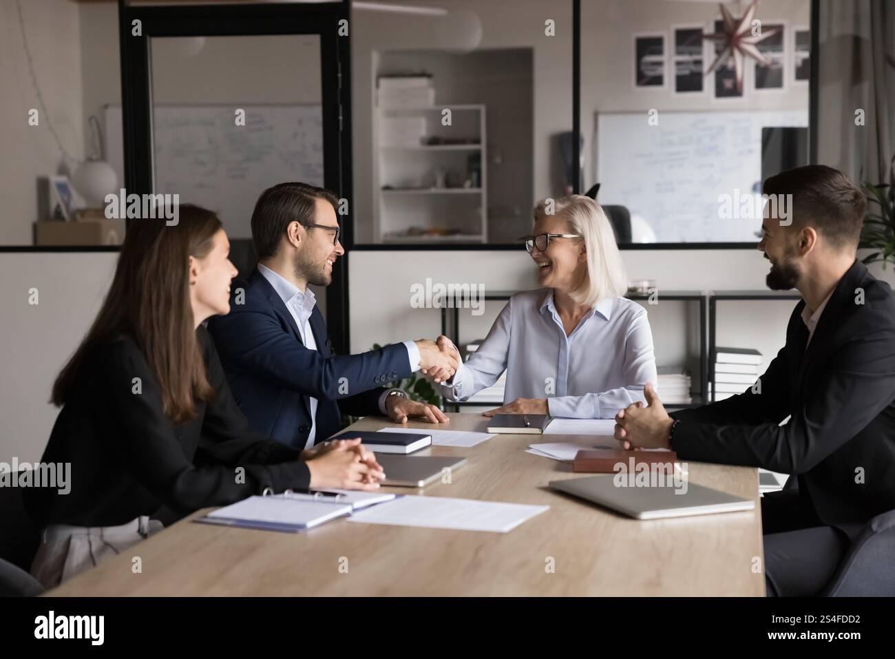 Two business partners shaking hands seated around office table Stock ...