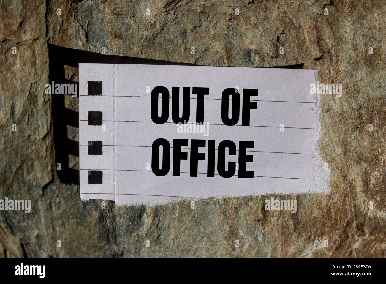 Out of office message written on ripped torn paper piece with stone ...