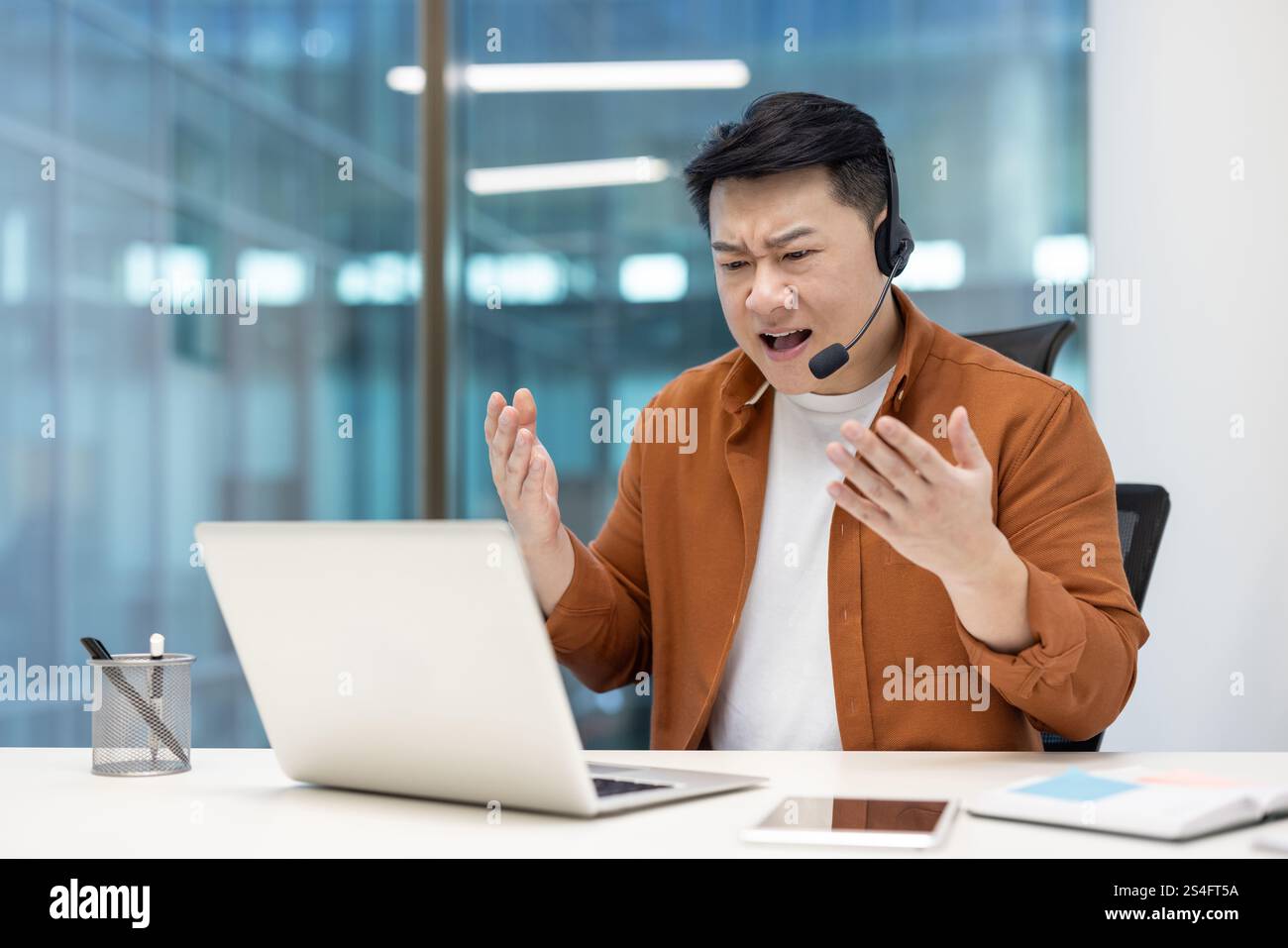 Angry man with headset talking while sitting at laptop inside office ...
