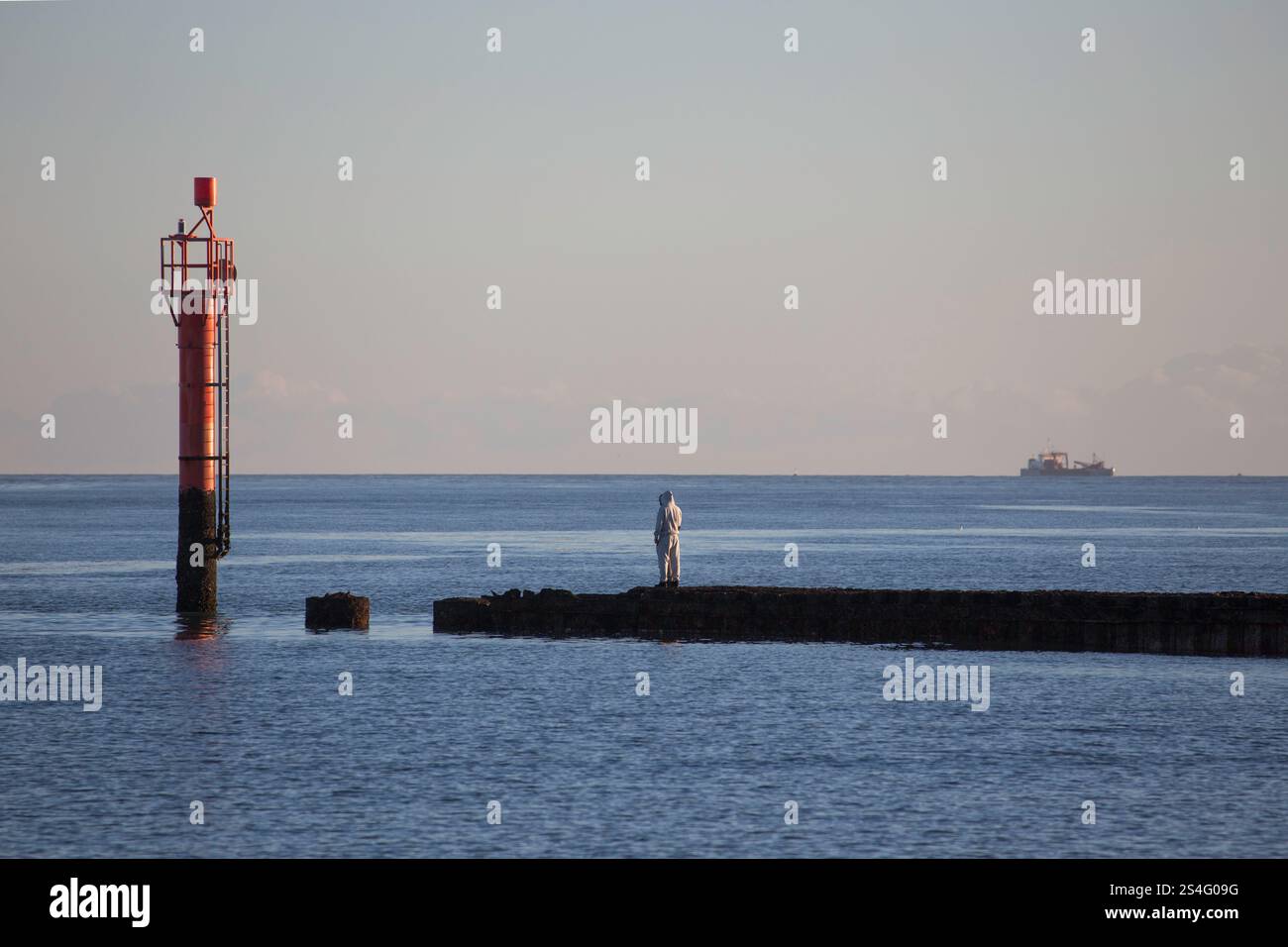 Lone man staring at a beach marker way out at sea of Portsmouth UK ...