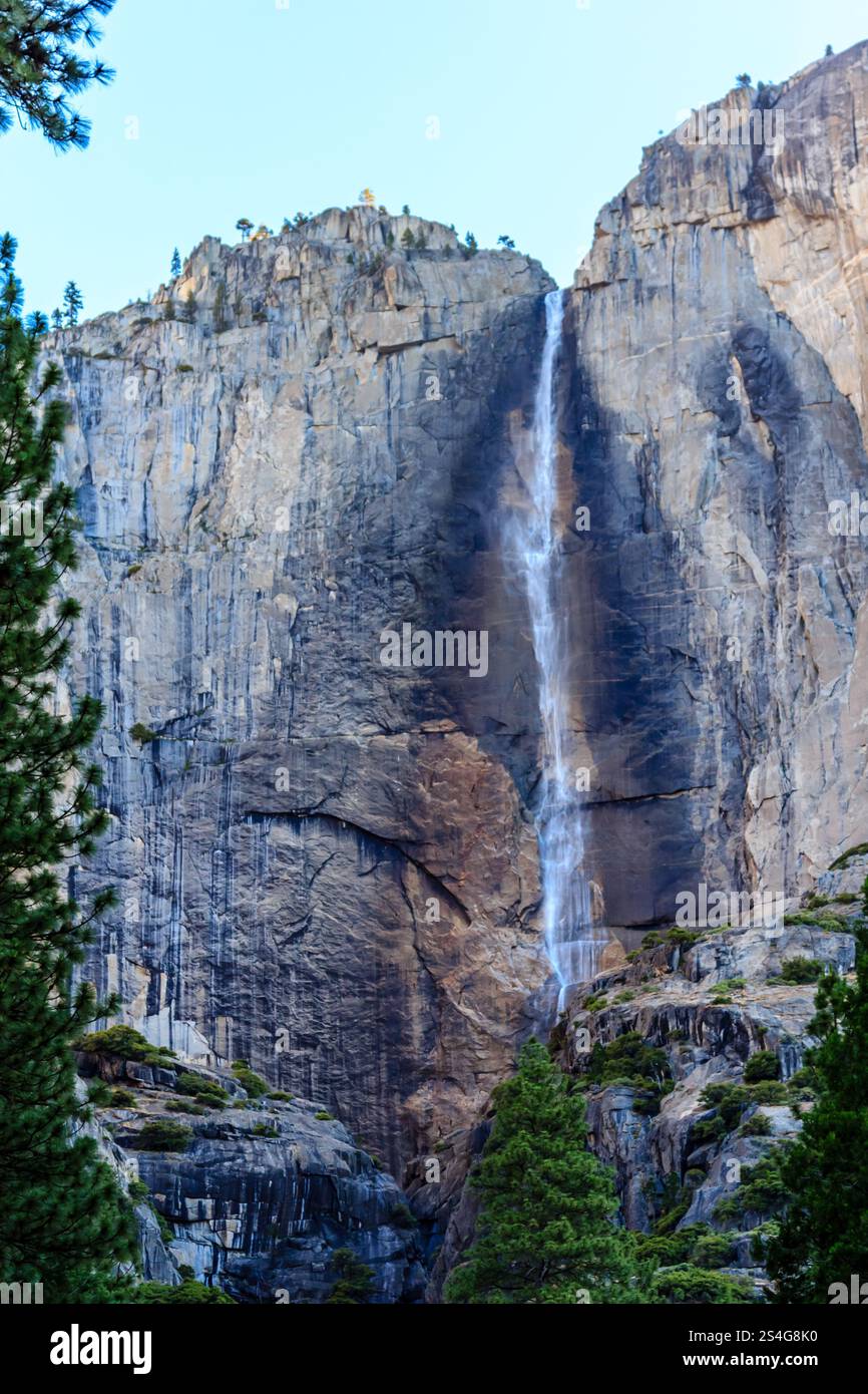 A waterfall cascades down a rocky cliff, surrounded by trees. The scene ...