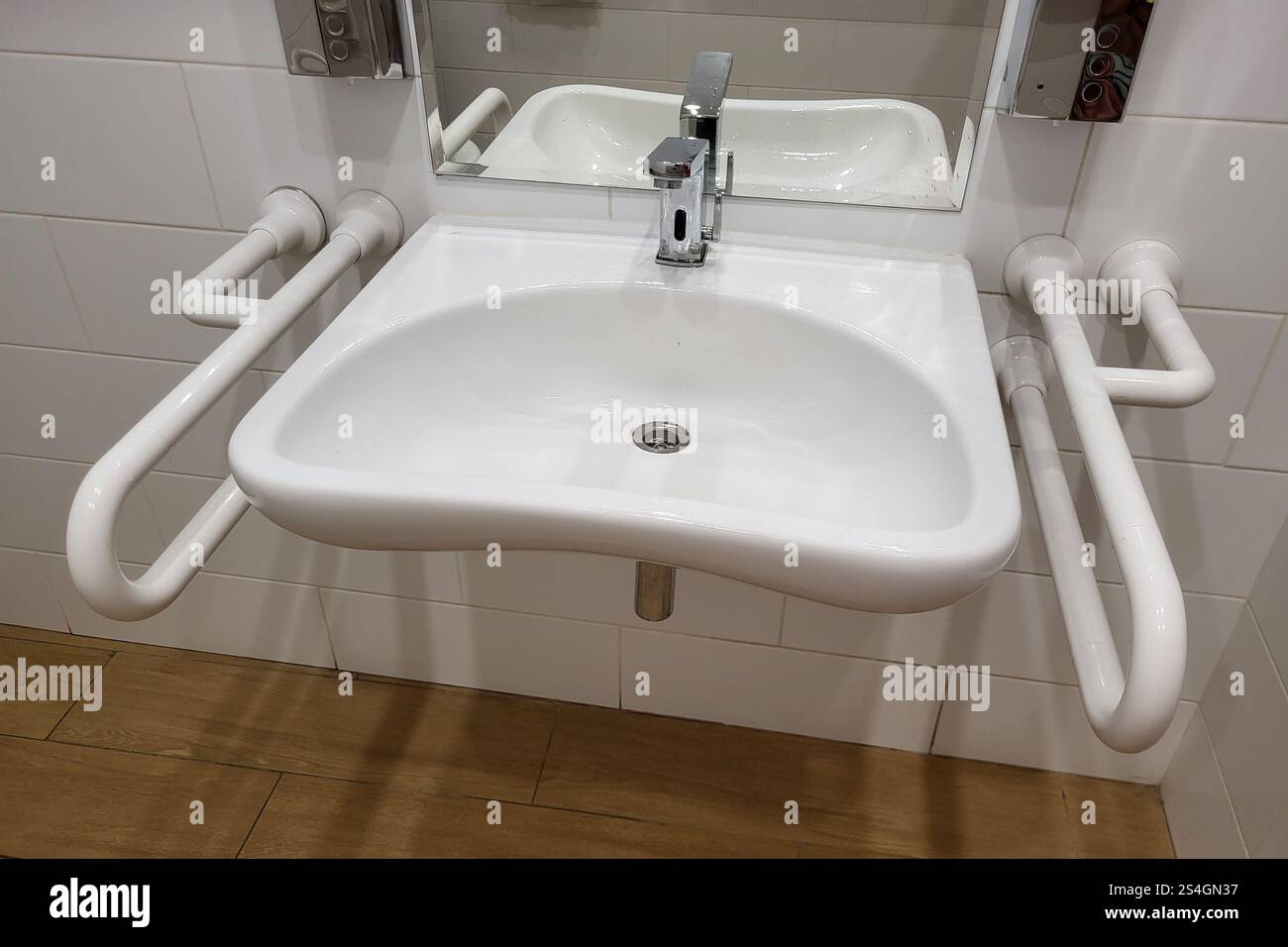 Wall-mounted white sink with chrome faucet and safety grab bars on both ...