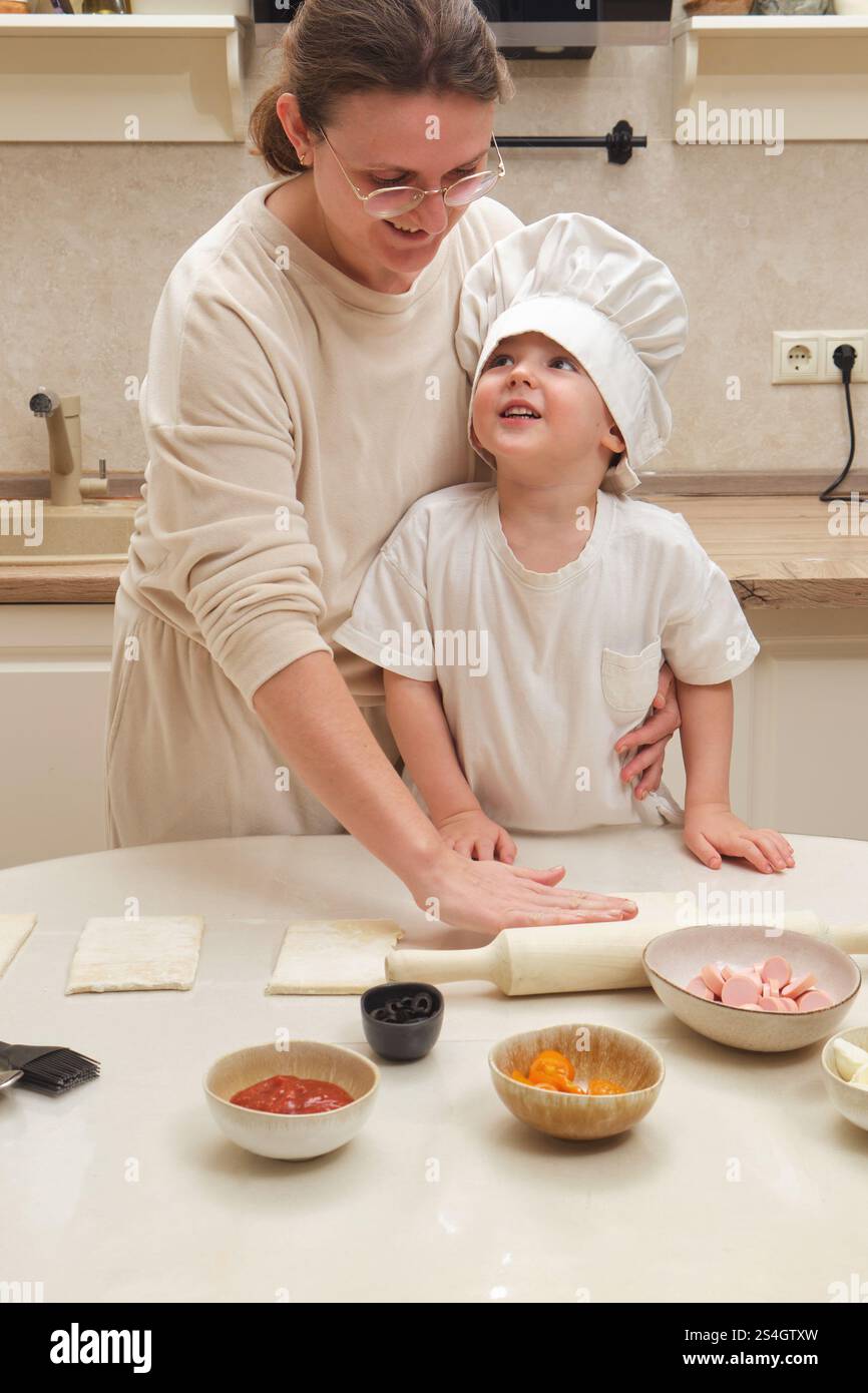 In the family kitchen, a mom is cooking pizza with her little boy ...