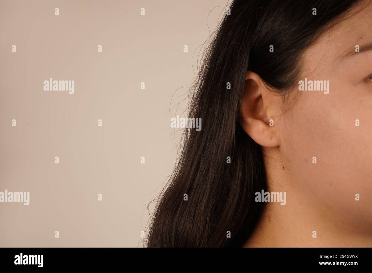 The ear of a woman is captured up close, with loose, dark hair softly ...