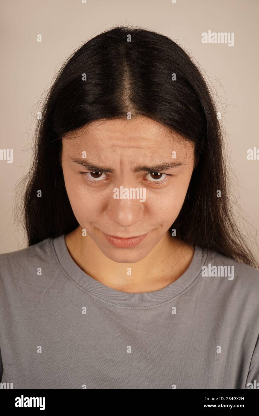 A young woman with furrowed brows displays an expression of seriousness ...