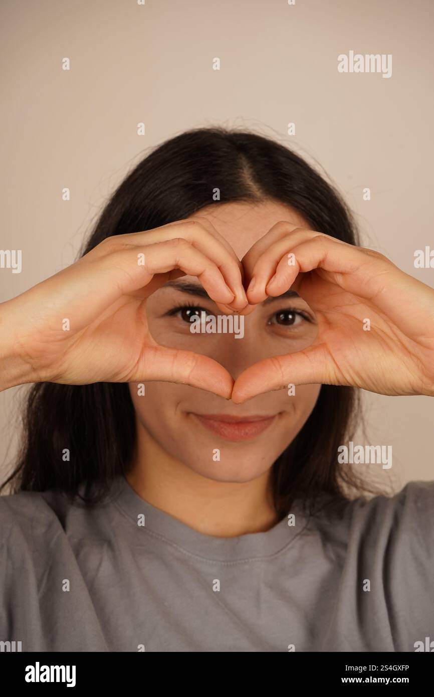 Smiling gently, the woman makes a heart gesture with her hands ...