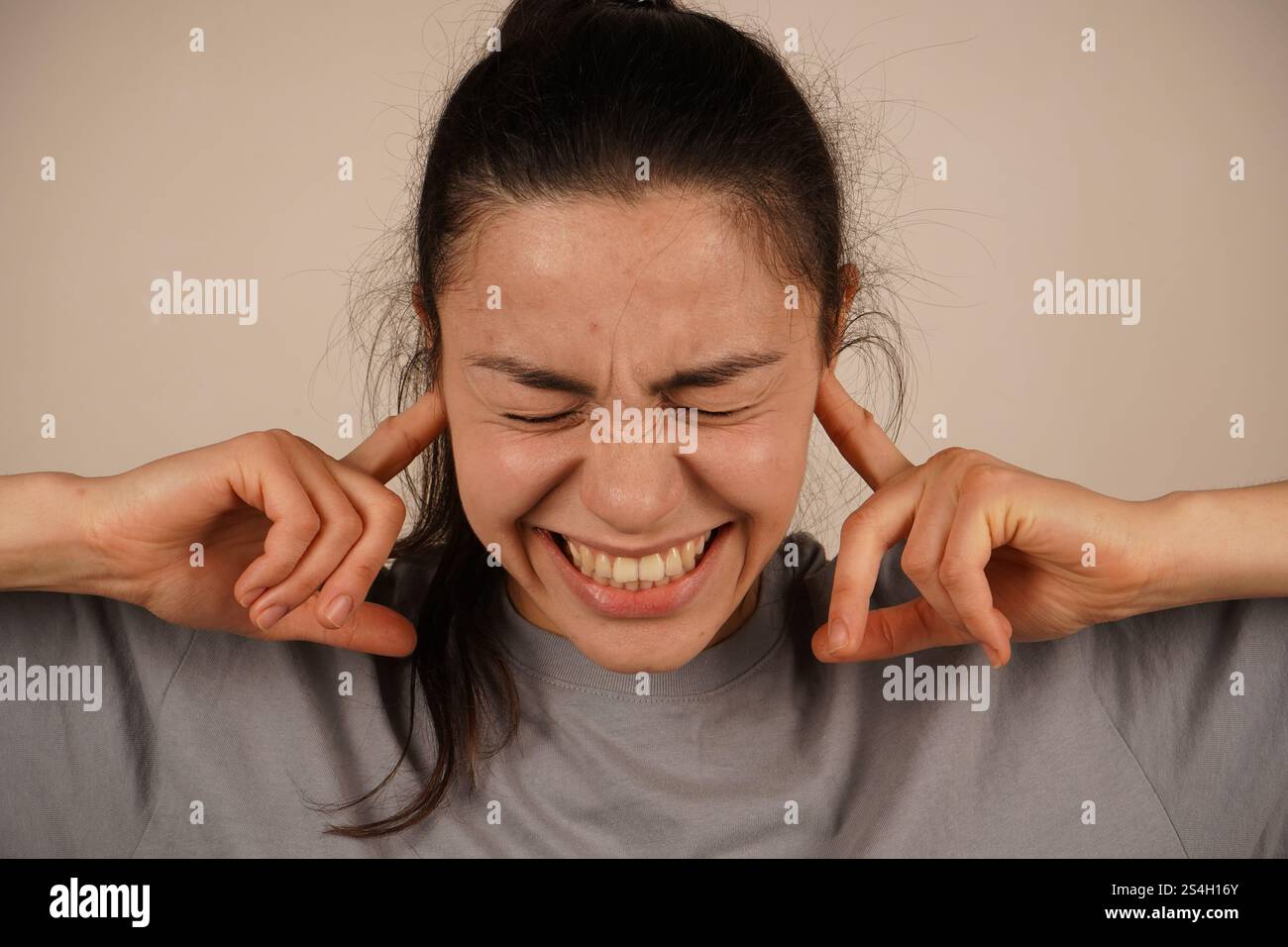 A woman covers her ears tightly with her fingers, isolating herself ...