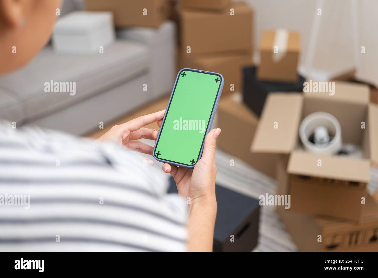Woman holds smartphone with green screen. cardboard boxes in a modern ...