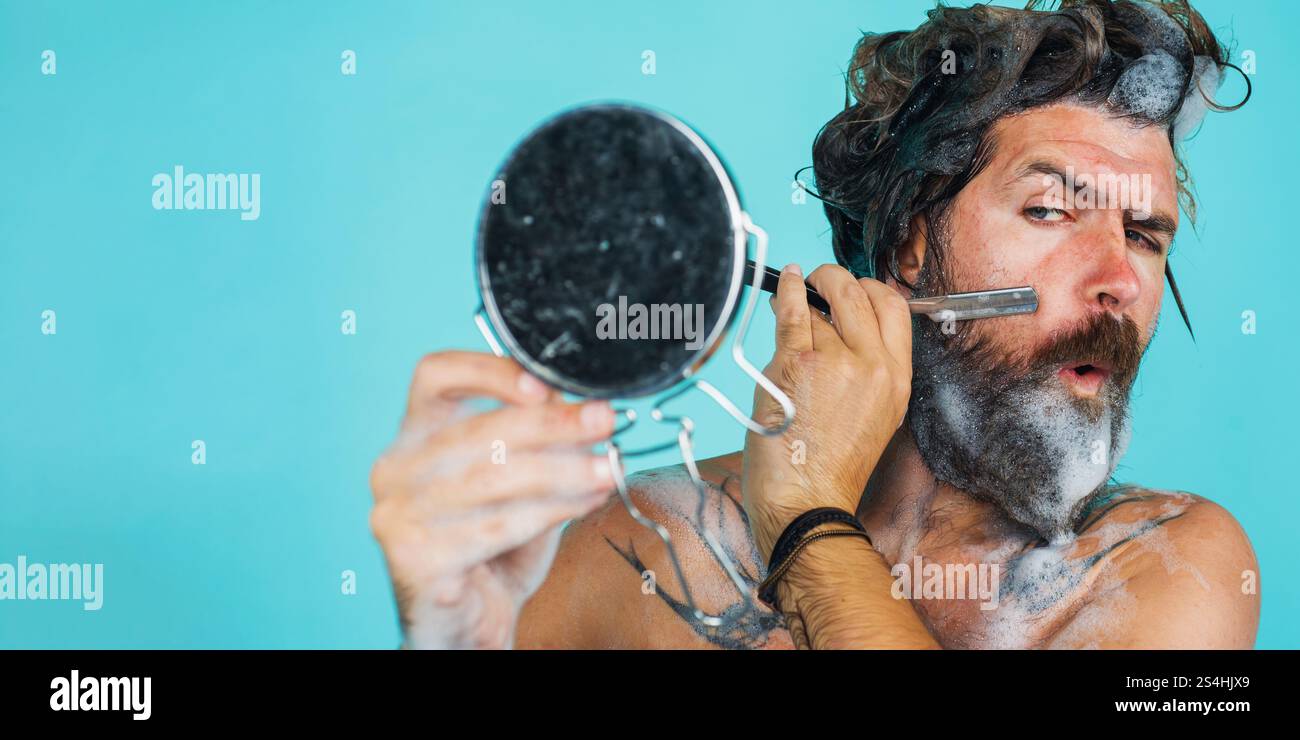 Bearded man shaving with straight razor looking at mirror. Morning routine. Beard care. Handsome ...