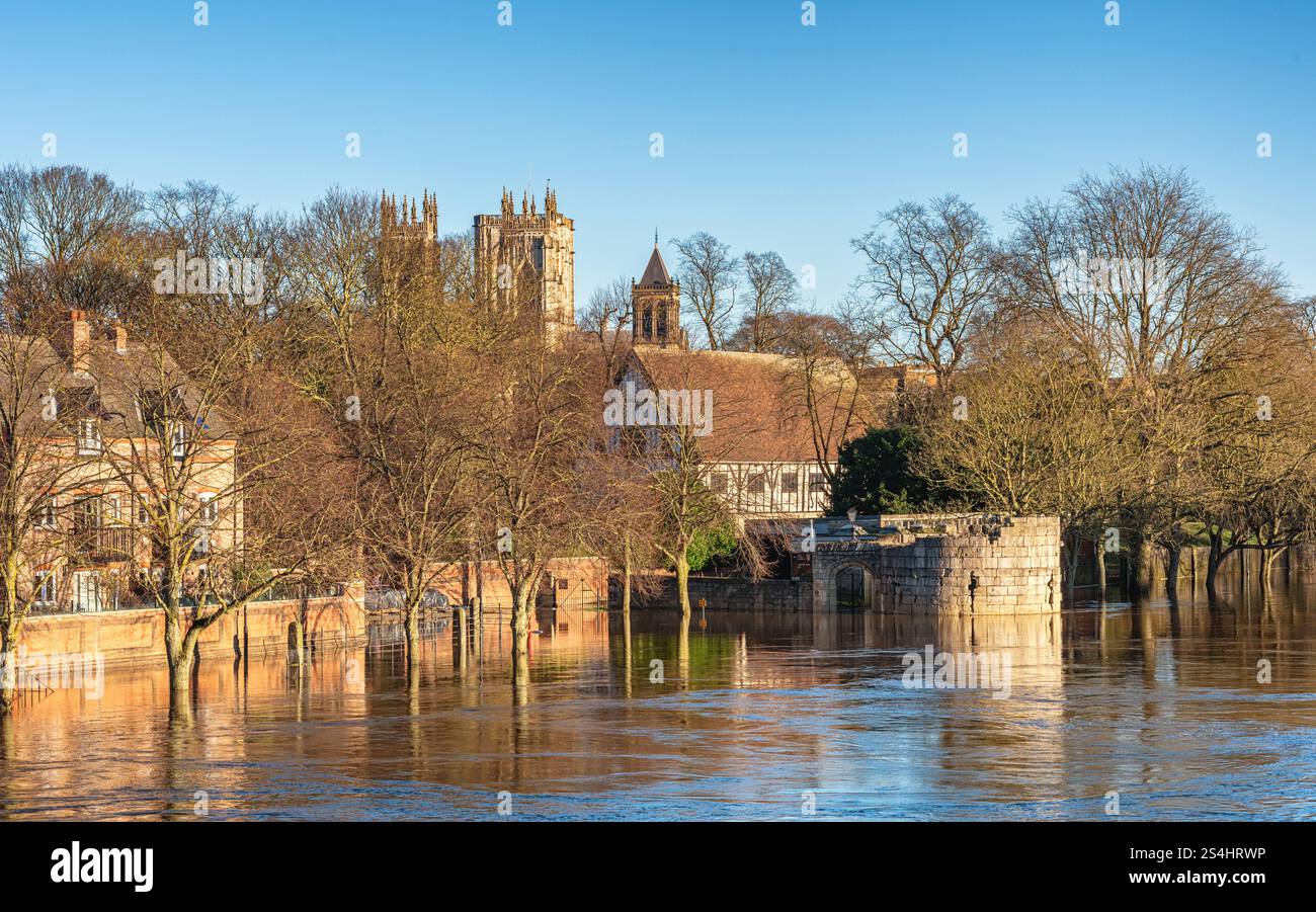 Buildings line a riverside in flood. The towers of a minster and a ...