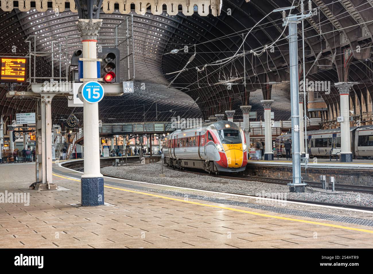 A railway station platform, lined by columns, curves, into a main concourse. A historic 19th ...