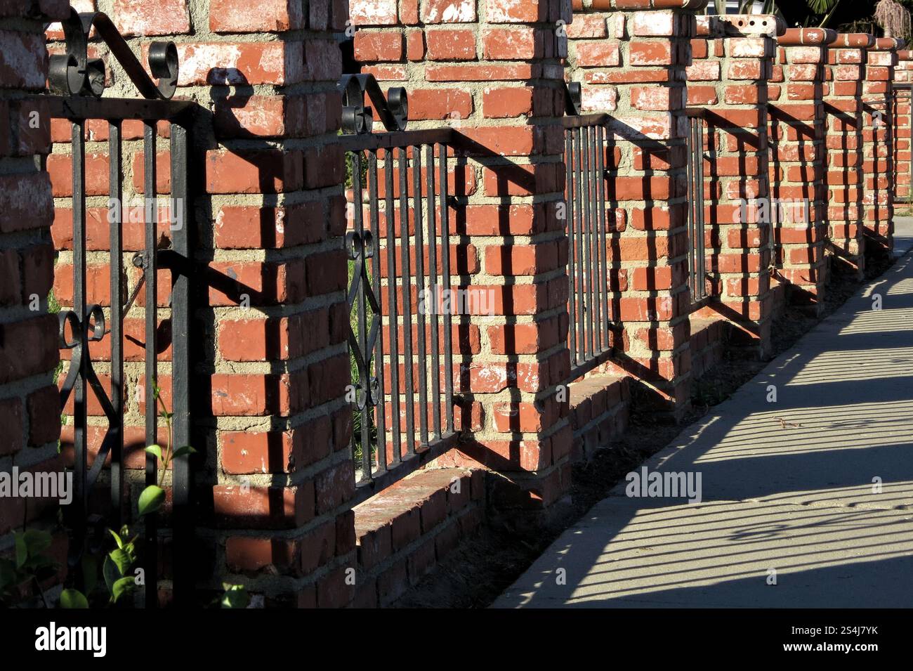 Black wrought iron fence with red brick posts are seen in a residential ...