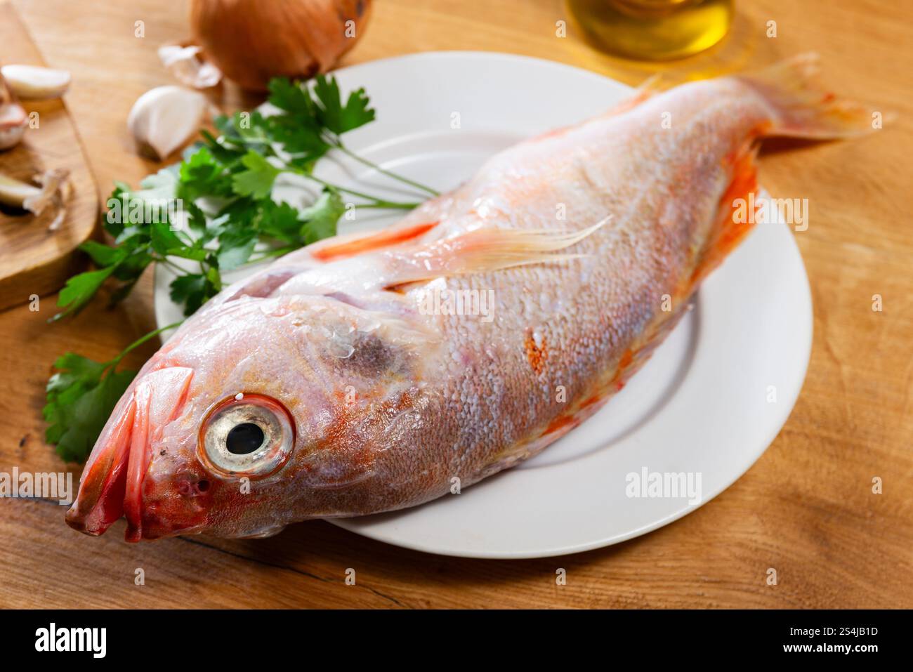 Raw whole red palometa fish with garlic and parsley on desk Stock Photo ...
