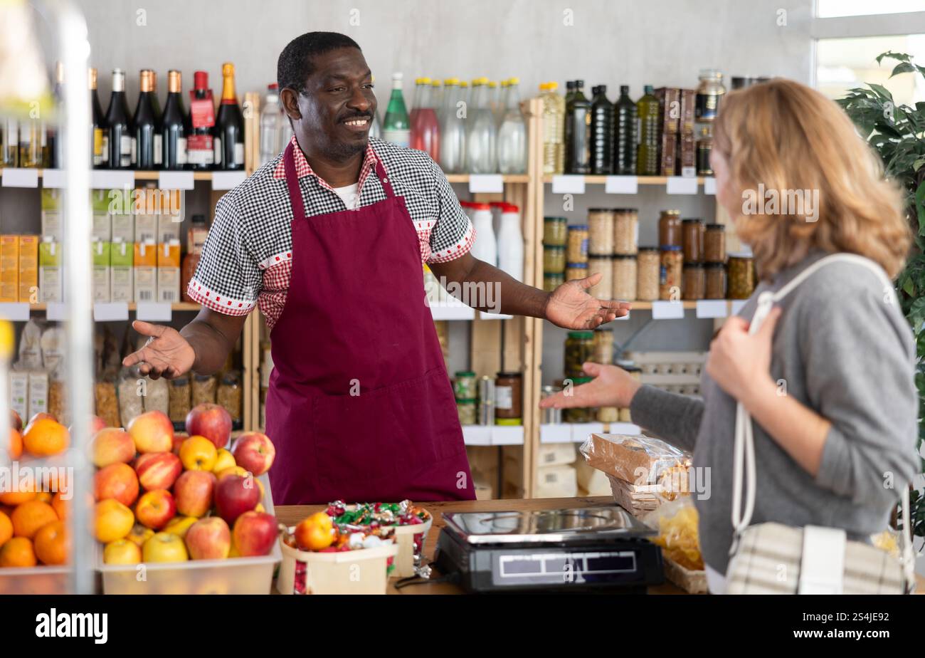 African man store clerk serves woman customer, sells something and ...